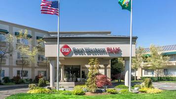 Entrada de um hotel Best Western com duas bandeiras, um jardim ajardinado e fachada de edifício moderna.