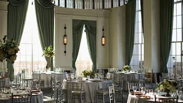 Uma sala de jantar formal com várias mesas redondas dispostas para uma refeição, cada uma com cadeiras e louças.