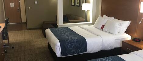Quarto de hotel com duas camas, uma escrivaninha, uma cadeira, um abajur e um relógio.