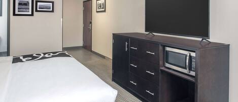 Quarto de hotel com cama, televisão de tela plana presa a um móvel e micro-ondas.