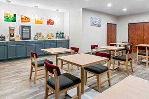 Uma sala de jantar moderna com mesas e cadeiras de madeira, um balcão com uma máquina de café e obras de arte nas paredes.