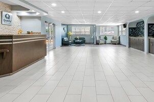 Uma área de recepção de hotel com balcão, espaço para sentar e uma janela grande.