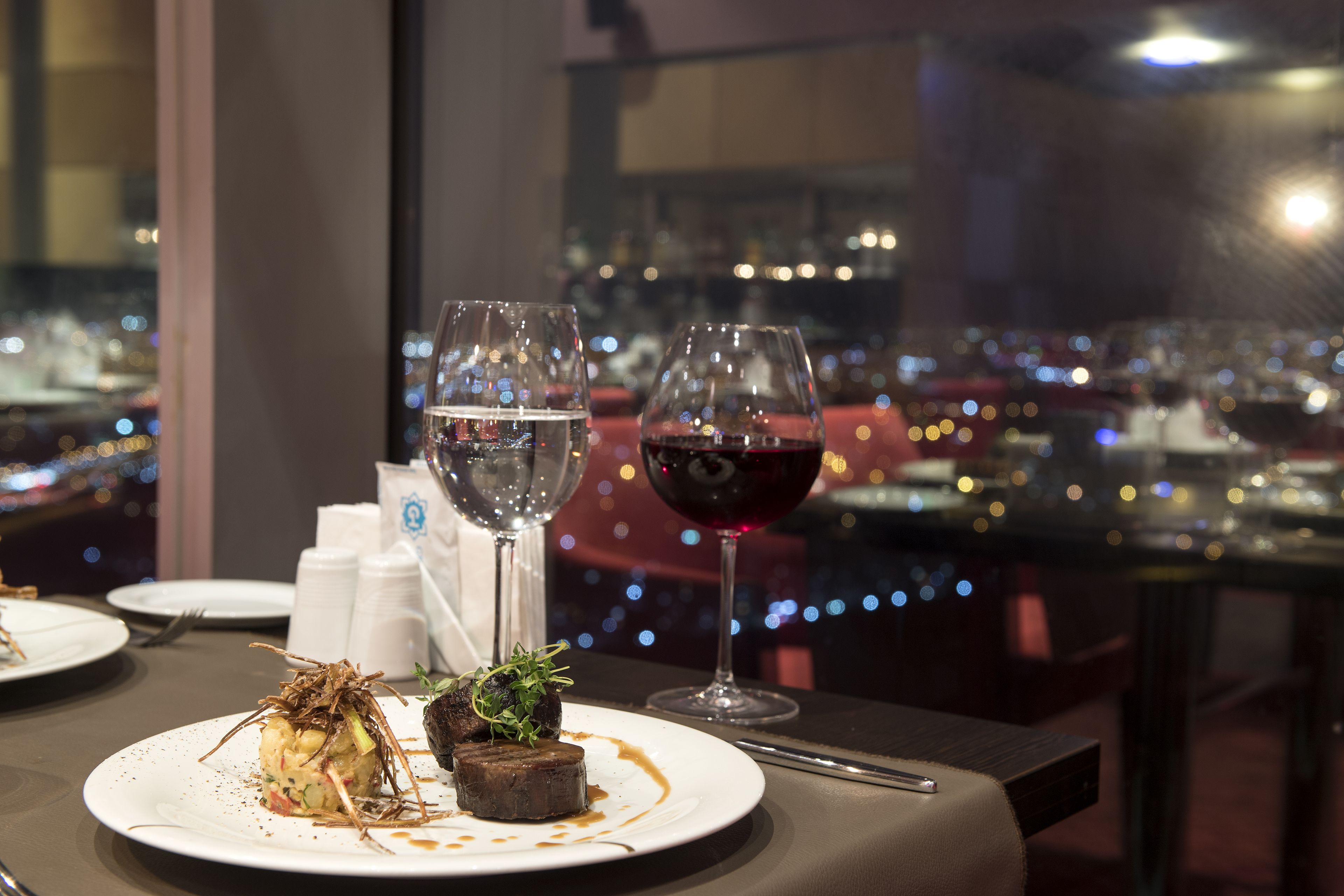 Uma mesa de jantar com sobremesa, duas taças de vinho e vista para a cidade ao fundo.
