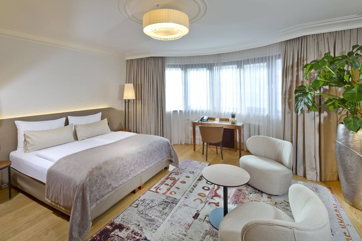 Quarto de hotel com uma cama grande, uma escrivaninha, uma cadeira e um vaso de plantas.