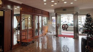 Um hall de hotel com piso de mármore polido, balcão de recepção, árvore de Natal e elevador de vidro.
