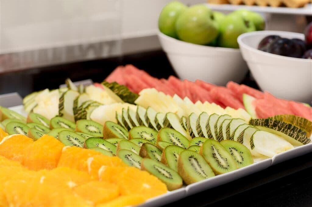 Uma bandeja com fatias de frutas, incluindo kiwi, manga, melancia e maçã.