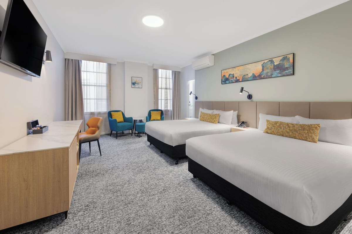 Quarto de hotel com duas camas, uma escrivaninha, uma televisão e um quadro na parede.