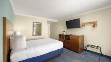 Quarto de hotel com uma cama, cômoda de madeira, televisão fixada na parede e um pequeno cabideiro.
