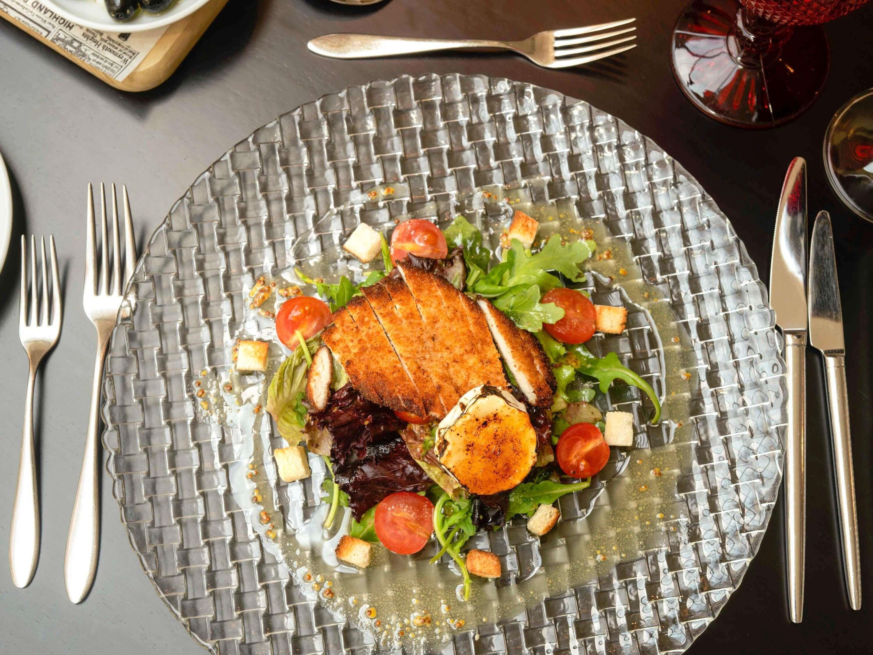 Um prato com peito de frango grelhado, salada e croutons.