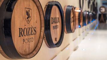 Fileira de barris de madeira com etiquetas, provavelmente para armazenamento de vinho, em ambiente interno bem iluminado.