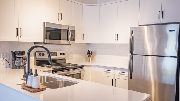 Uma cozinha moderna com armários brancos, eletrodomésticos de aço inoxidável, forno embutido e uma geladeira grande.
