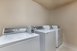Uma lavanderia com duas máquinas de lavar roupa frontais e uma secadora.