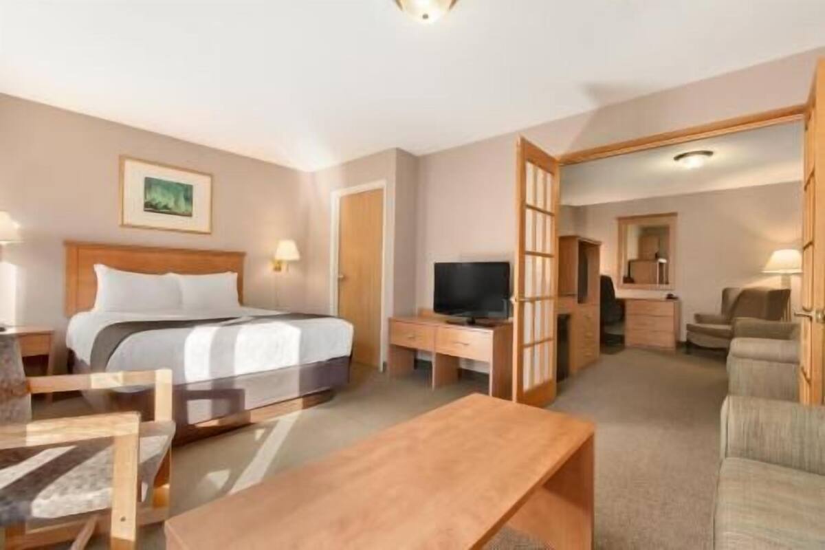 Quarto de hotel com cama, escrivaninha, televisão, poltrona e sofá.