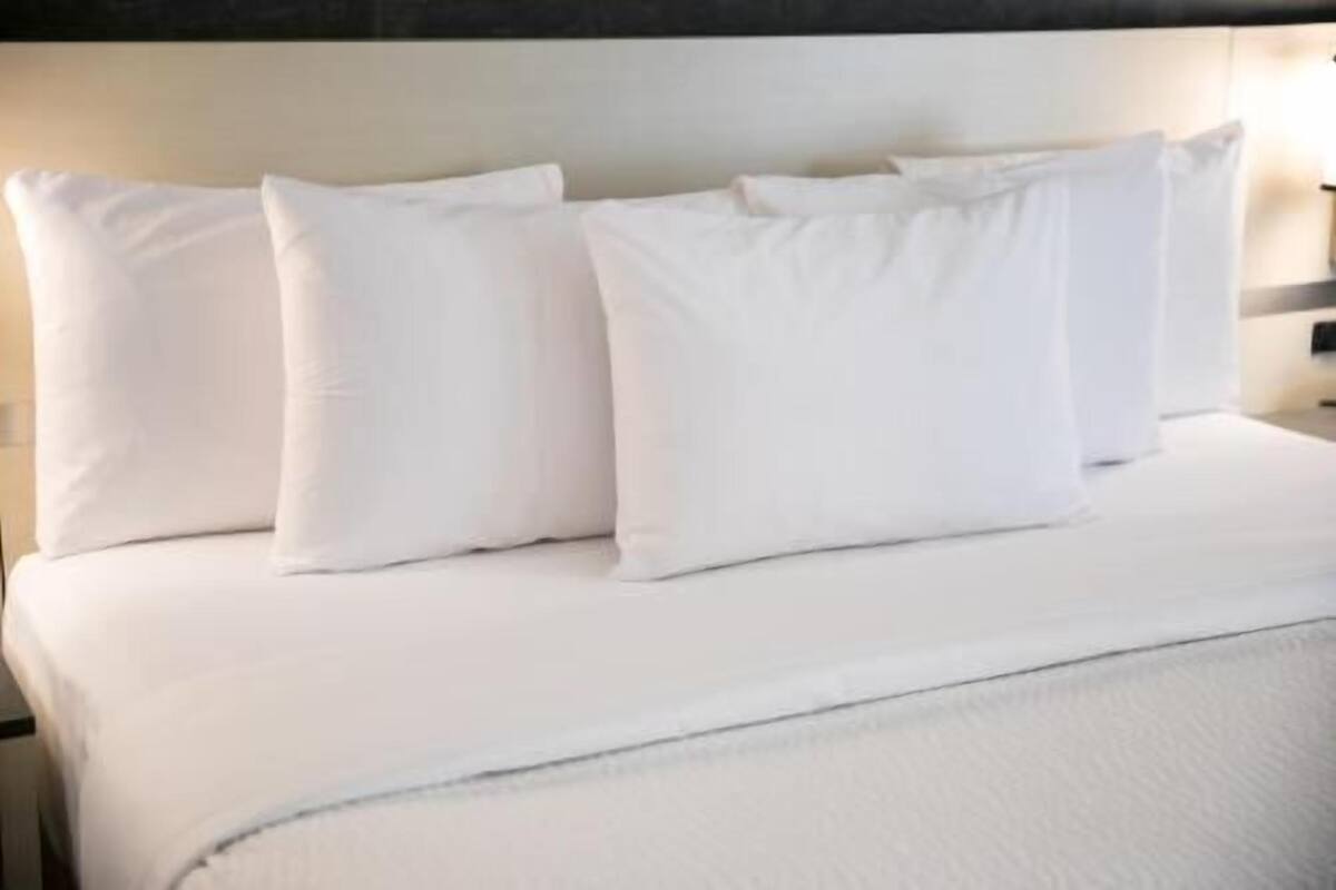 Cama bem arrumada com lençóis e almofadas brancos, design de quarto limpo e minimalista.