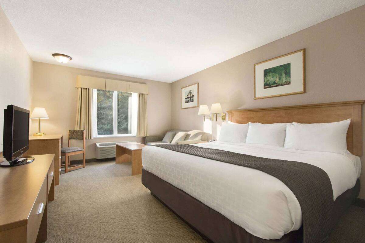Quarto de hotel com cama, escrivaninha, cadeira, televisão e duas luminárias.