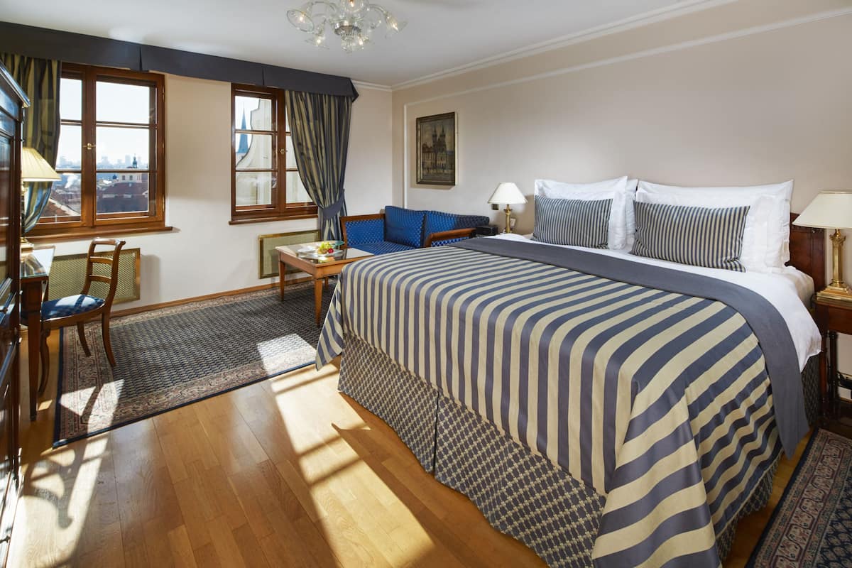 Quarto de hotel com uma cama grande, uma escrivaninha, uma cadeira, uma janela com cortinas e vista para a cidade.