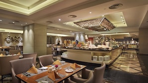 Uma área de refeições de hotel moderna, com serviço de buffet, várias mesas de jantar e um bar central.