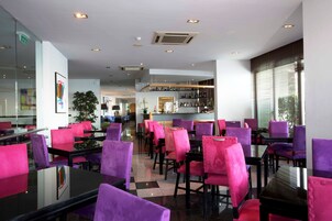 Um hall de hotel moderno com cadeiras roxas e rosa, uma área de bar e um balcão de recepção.