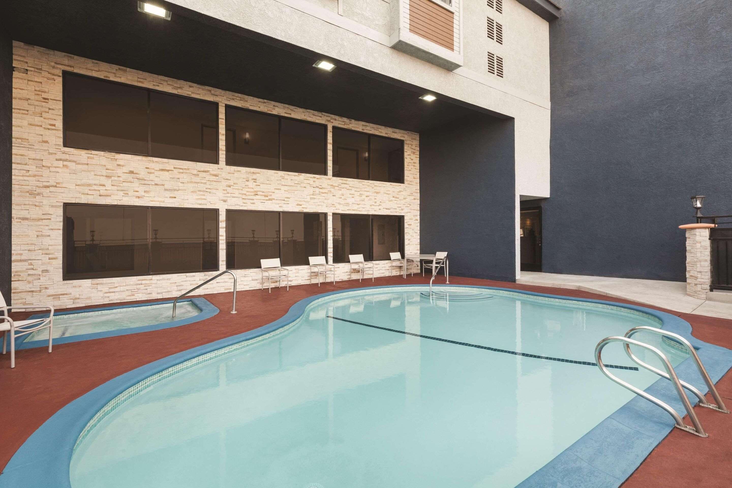 Área de piscina com parede de tijolos, várias janelas e área de estar ao ar livre.