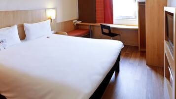 Quarto de hotel com uma cama grande, uma escrivaninha, uma cadeira e uma janela com cortinas.