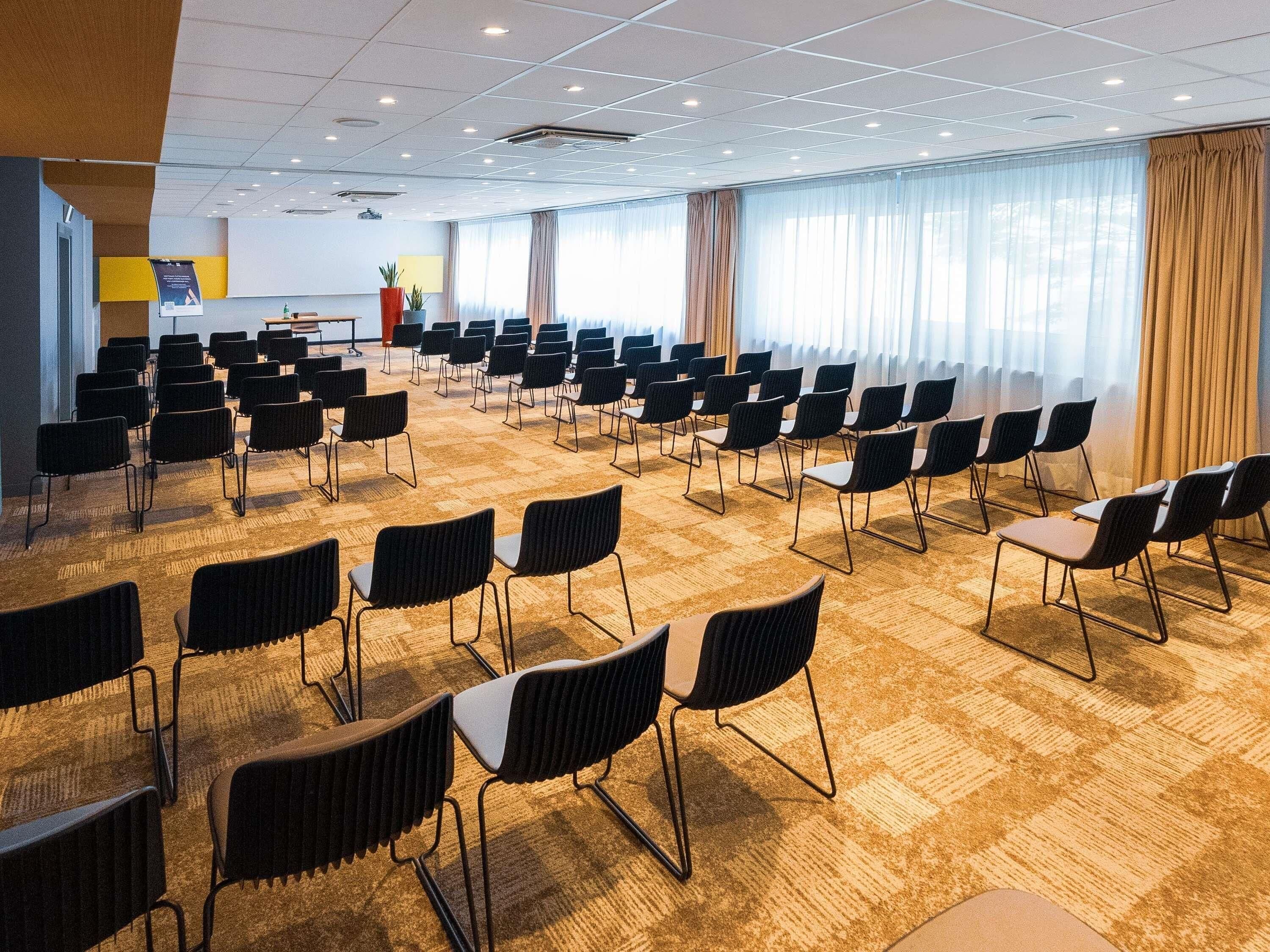 Uma sala de conferências com fileiras de cadeiras, um púlpito e piso coberto de carpete.
