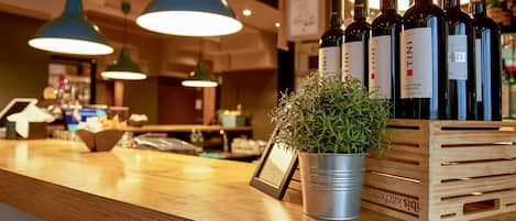 Uma área de bar com balcão de madeira, luminárias pendentes azuis, uma planta em vaso e uma caixa com garrafas de vinho.