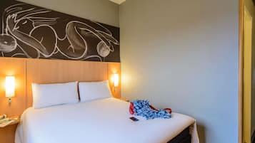 Quarto de hotel com cama grande, duas luminárias de cabeceira, uma obra de arte na parede e uma mala sobre a cama.