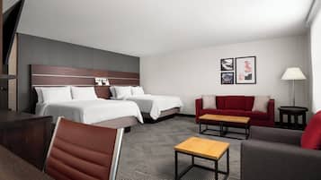 Quarto de hotel com duas camas, um sofá vermelho, uma mesa de madeira e uma luminária.