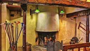 Um interior rústico com lareira, vigas de madeira e uma estante de metal com diversas ferramentas.