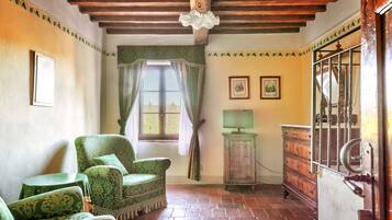 Quarto com teto de madeira, poltronas com estampa verde, um armário de madeira e uma janela com cortinas.