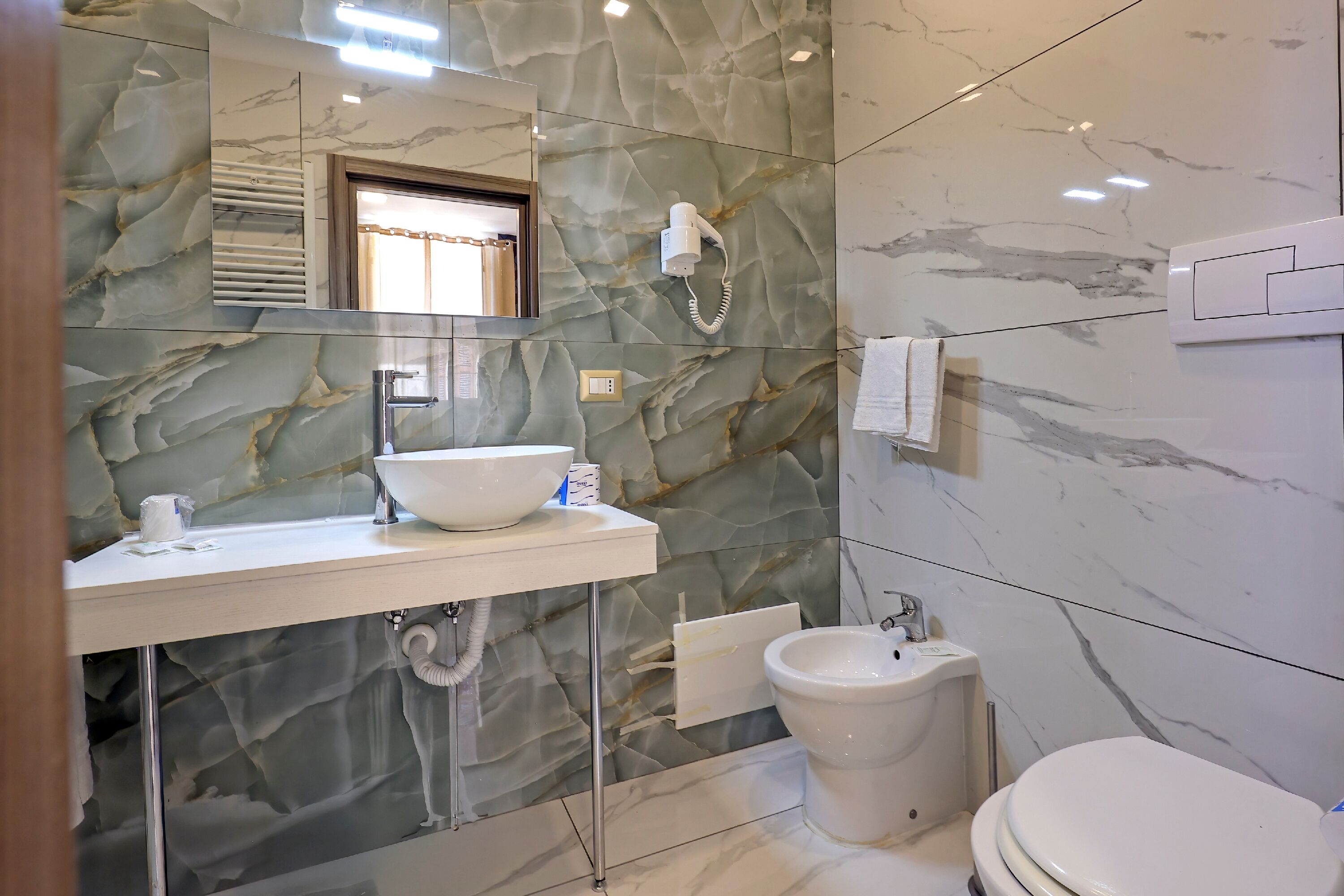 Uma casa de banho moderna com painel de parede em mármore, uma sanita branca, chuveiro manual, bidé e sanita.