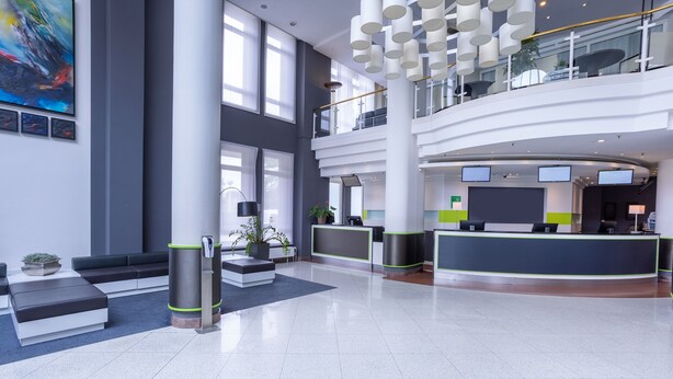 Um hall amplo com balcão de recepção, área de estar e escadaria para um andar superior.