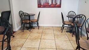 Uma área de refeições com quatro mesas e cadeiras, um quadro na parede e piso ladrilhado.