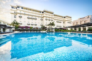 Uma grande piscina ao ar livre com áreas de estar e um edifício de hotel ao fundo.