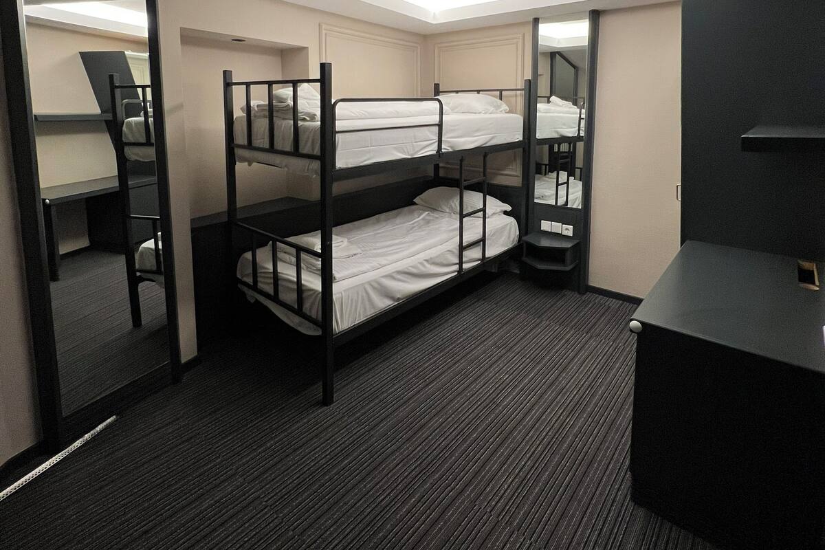 Quarto de hotel compacto com beliches, escrivaninha e espelho.