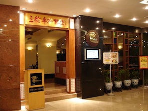 Entrada de hotel com um letreiro asiático tradicional, um balcão de recepção e plantas em vasos.