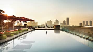 Piscina infinita no terraço com vista para o horizonte urbano, área de estar ao ar livre e guarda-sóis.