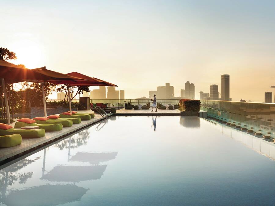 Piscina infinita no terraço com vista para o horizonte urbano, área de estar ao ar livre e guarda-sóis.