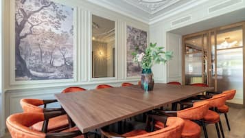 Uma sala de jantar com uma mesa de madeira comprida, cadeiras estofadas em laranja e grandes pinturas penduradas na parede.