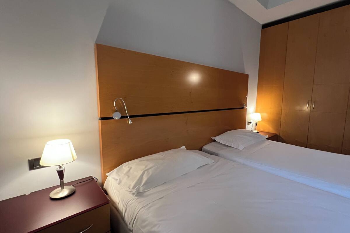 Quarto de hotel com cama, luminárias de cabeceira, painel de cama em madeira e um guarda-roupa.