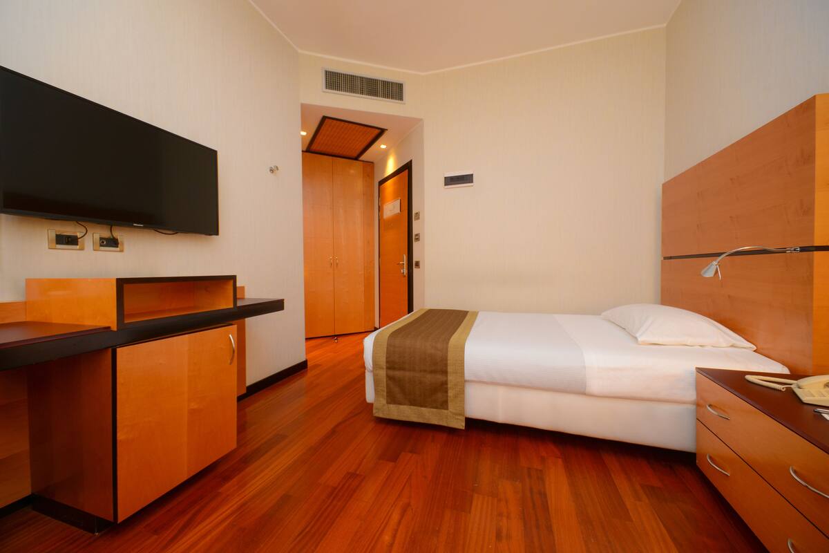 Quarto de hotel com cama, escrivaninha, televisão e guarda-roupa de madeira.