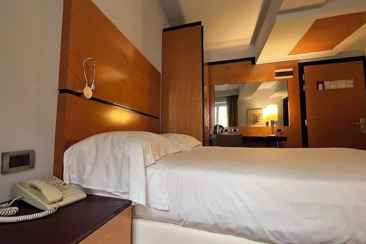 Quarto de hotel com cama, telefone ao lado, espelho e porta.