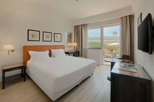 Quarto de hotel com cama grande, mesa de trabalho com televisão de tela plana e varanda com vista.