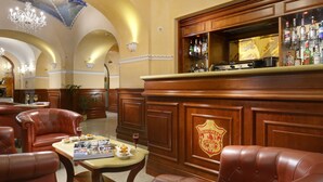 Uma área de bar com cadeiras de couro, balcão com garrafas de bebidas e um candelabro.