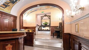 Um amplo hall de entrada com pisos de mármore, painéis de madeira e uma escadaria que leva a um andar superior.