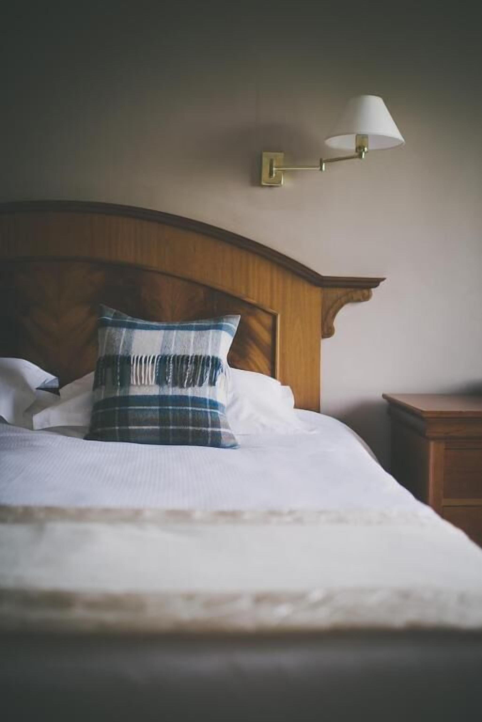 Cama bem arrumada com cabeceira de madeira, luminária de cabeceira e mesa de cabeceira de madeira.