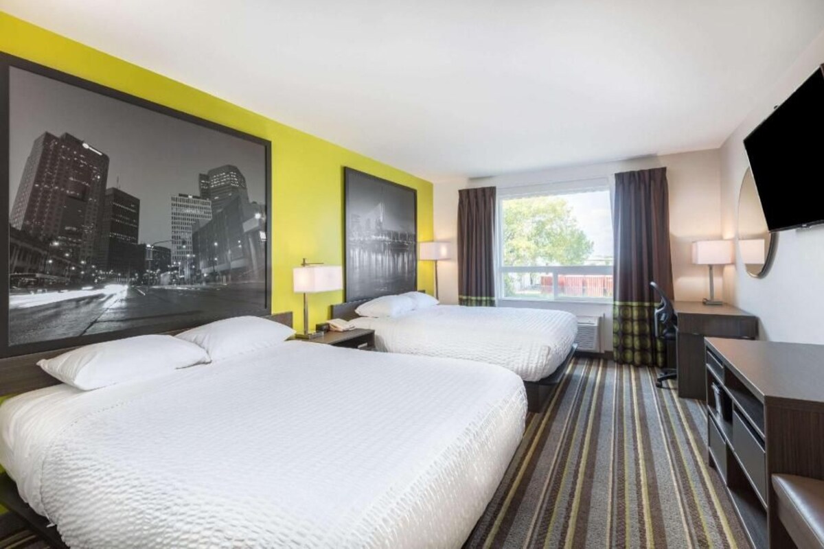 Quarto de hotel com duas camas, uma pintura grande da paisagem urbana, uma televisão e uma janela com cortinas.