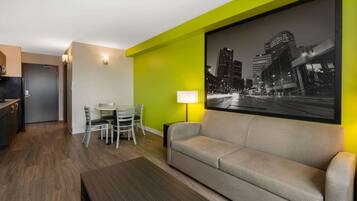 Quarto de hotel moderno com área de refeições, um sofá e uma pintura de paisagem urbana.