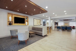 Um lobby moderno de hotel com televisão de tela plana, área de estar e espaço para refeições.