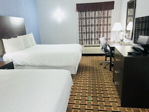 Quarto de hotel com duas camas, uma escrivaninha, uma cadeira, televisão e janela com cortinas estampadas.